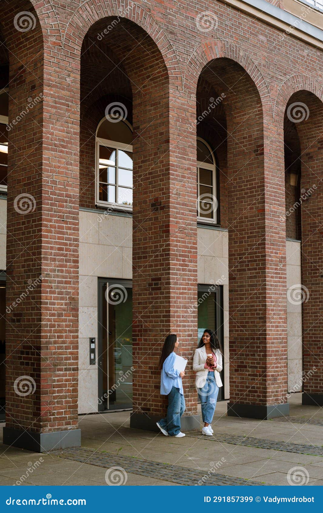 Two Multinational Women Talking while Standing by Building Outdoors ...