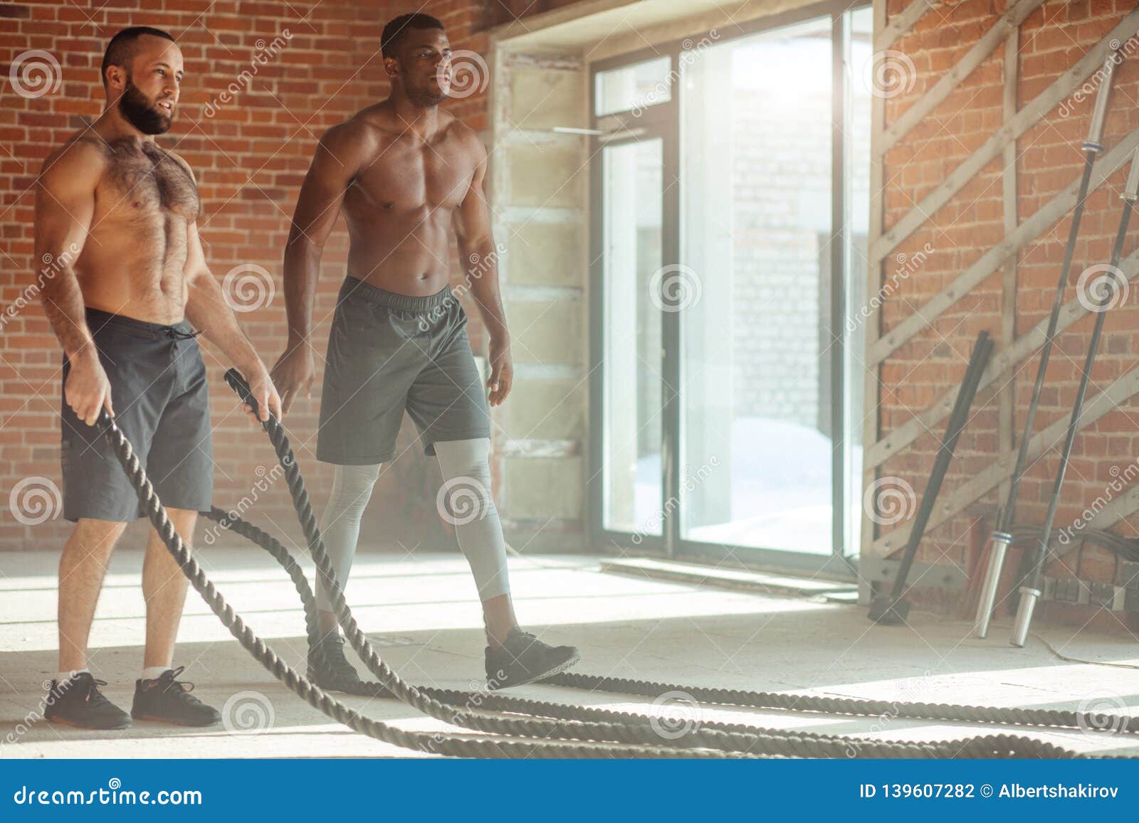 Two Multiethnic Bare Chest Sportsmen Exercising with Battle Ropes at ...