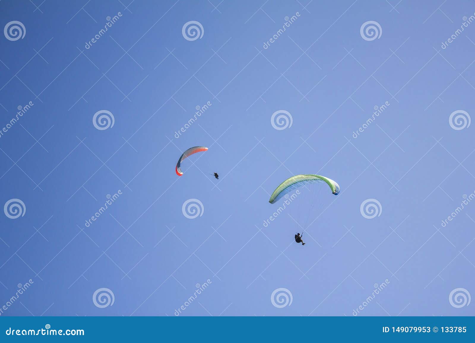 Two Paragliders on Colored Parachutes Fly Against a Clear Blue Sky ...