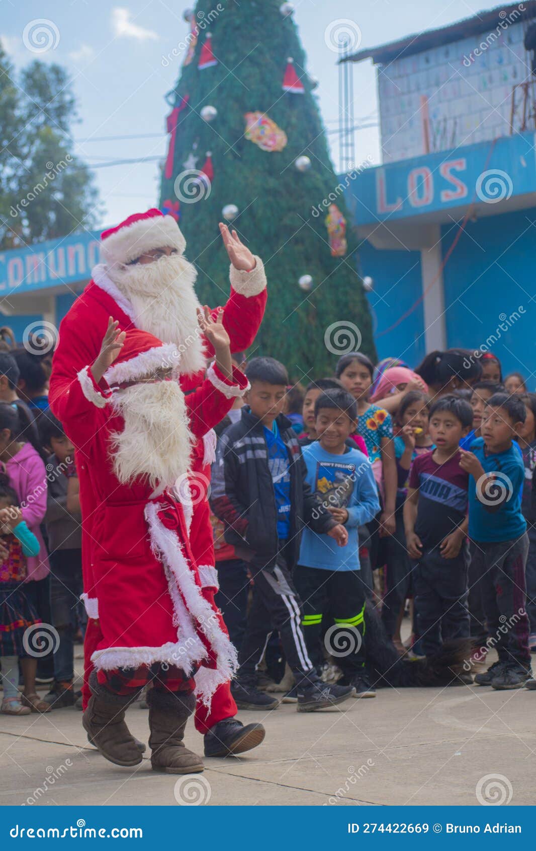 Two Santa Clauses Dancing in Front of Indigenous Children with a Tree ...