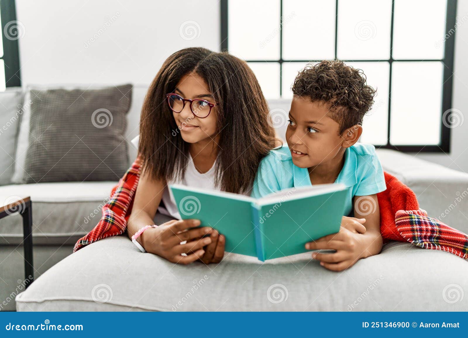 Two Siblings Lying on the Sofa Reading a Book Smiling Looking To the ...