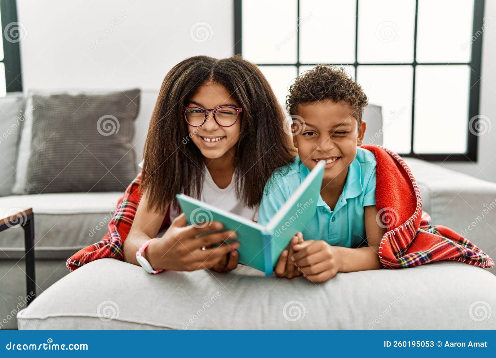 Two Siblings Lying on the Sofa Reading a Book Winking Looking at the ...