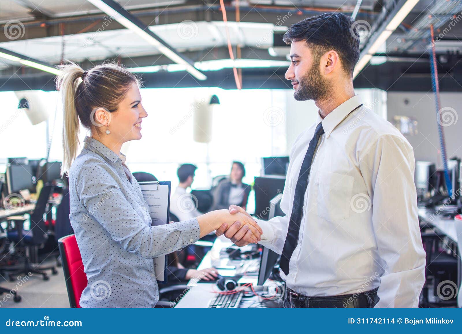Two Smiling Business People Shaking Hands Together while Standing in an ... Two Smiling Business People Shaking Hands Together while Standing in an ...