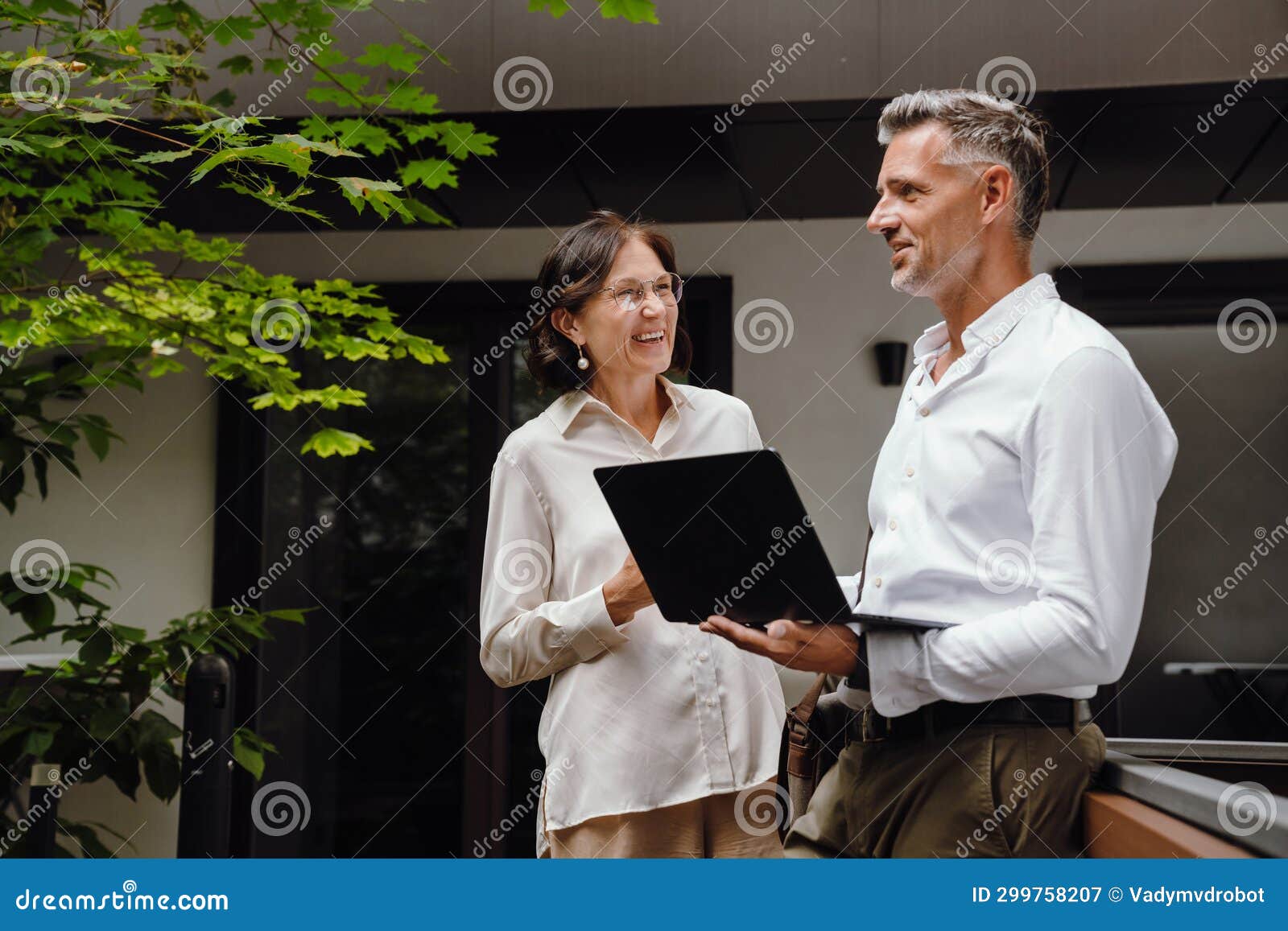 Two Smiling Business People Working on Laptop while Standing Outside ... Two Smiling Business People Working on Laptop while Standing Outside ...