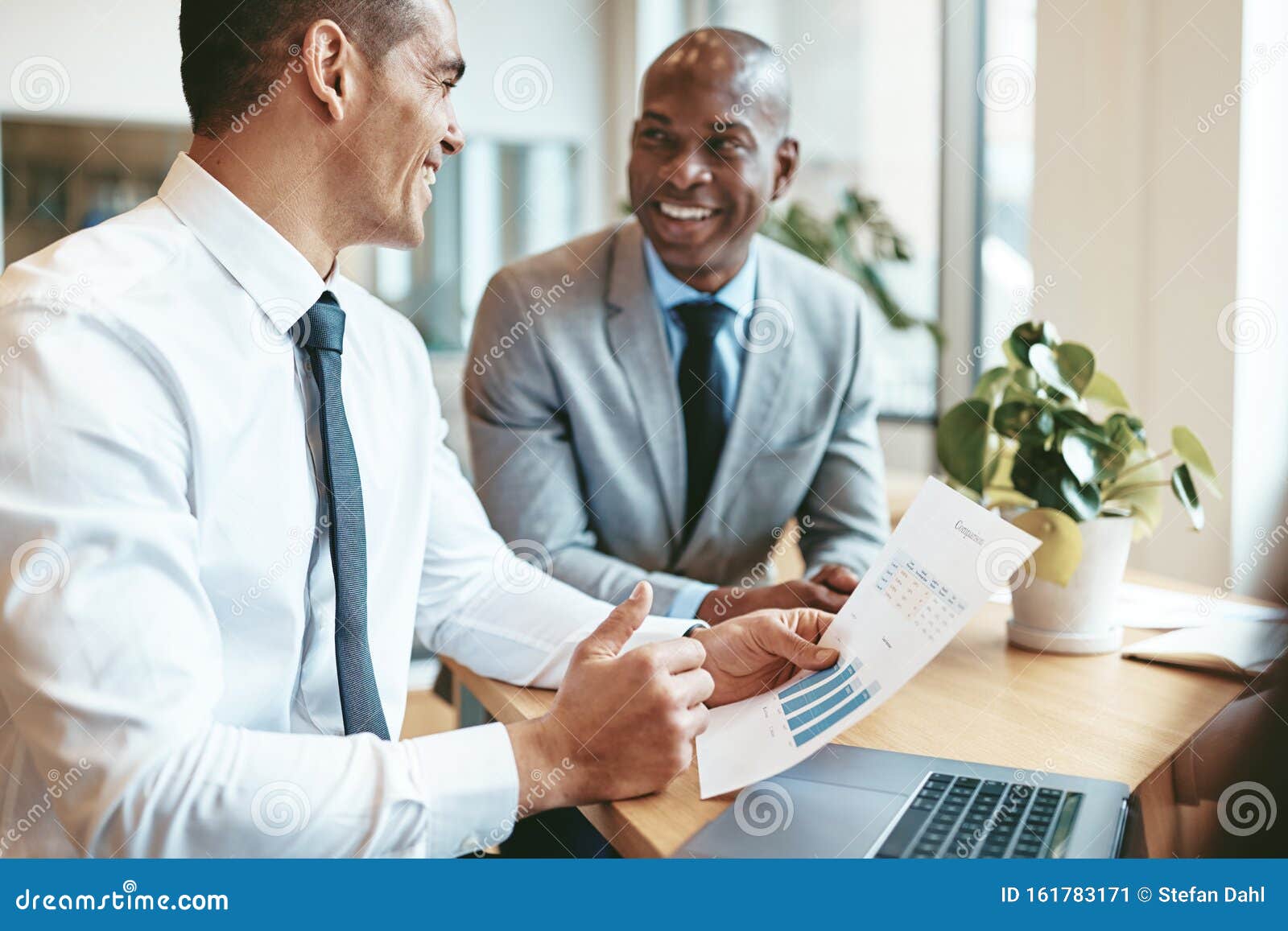 Two Smiling Diverse Businessmen Discussing Graphs Together in an Stock ... Two Smiling Diverse Businessmen Discussing Graphs Together in an Stock ...