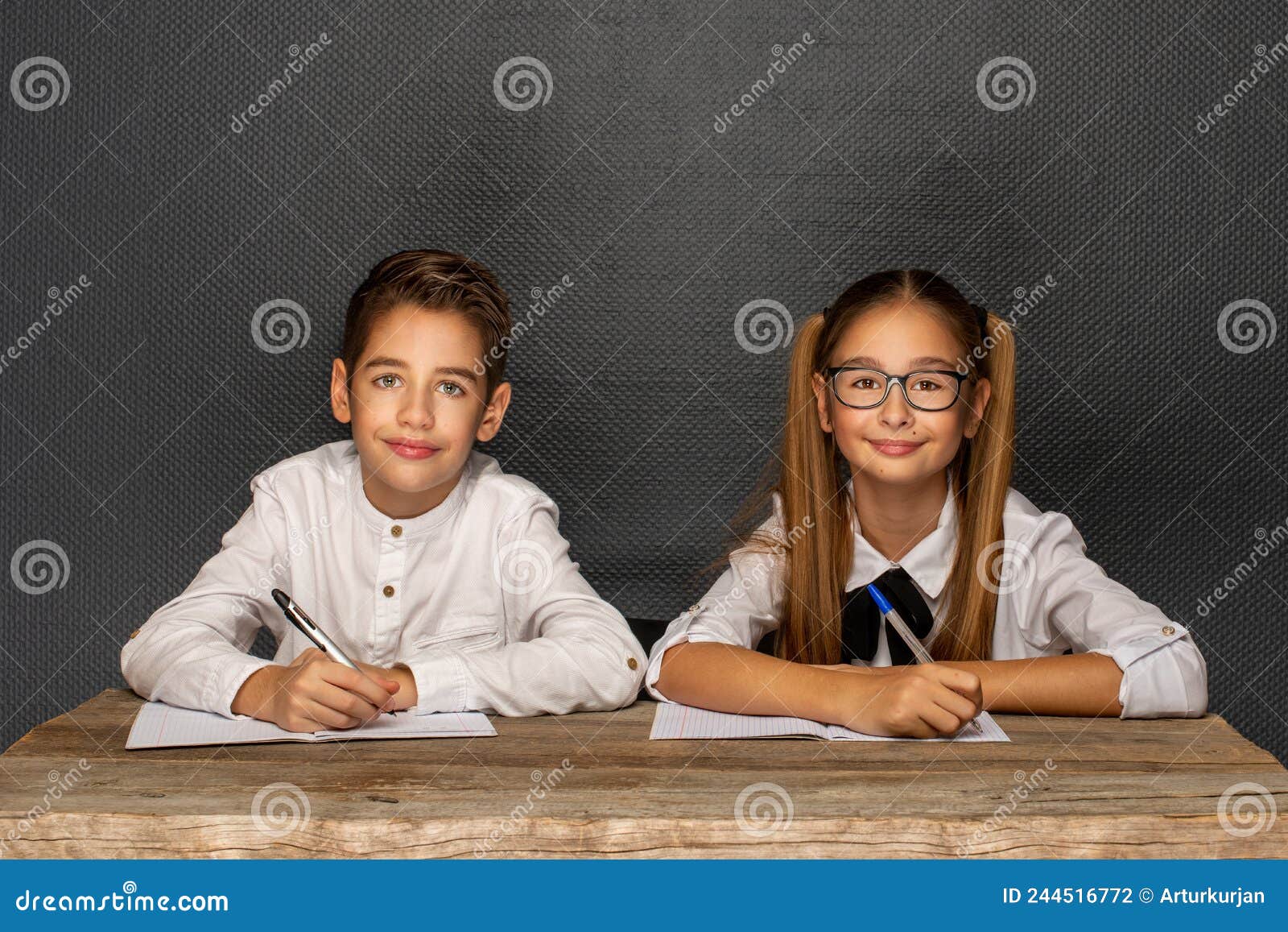 Two Smiling Kids at the Table Write with Pen, on Black Wall Stock Photo ...