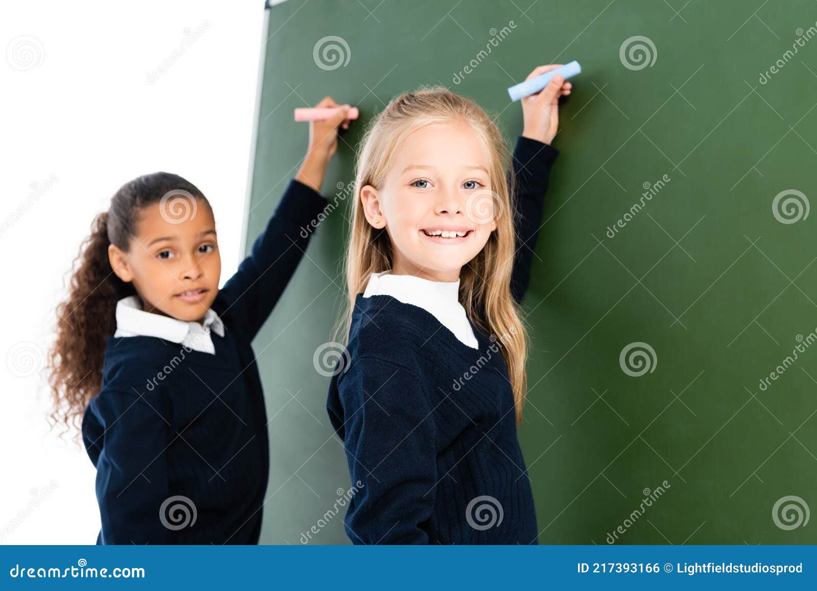 Two Smiling Multicultural Schoolgirls Writing on Chalkboard while ...