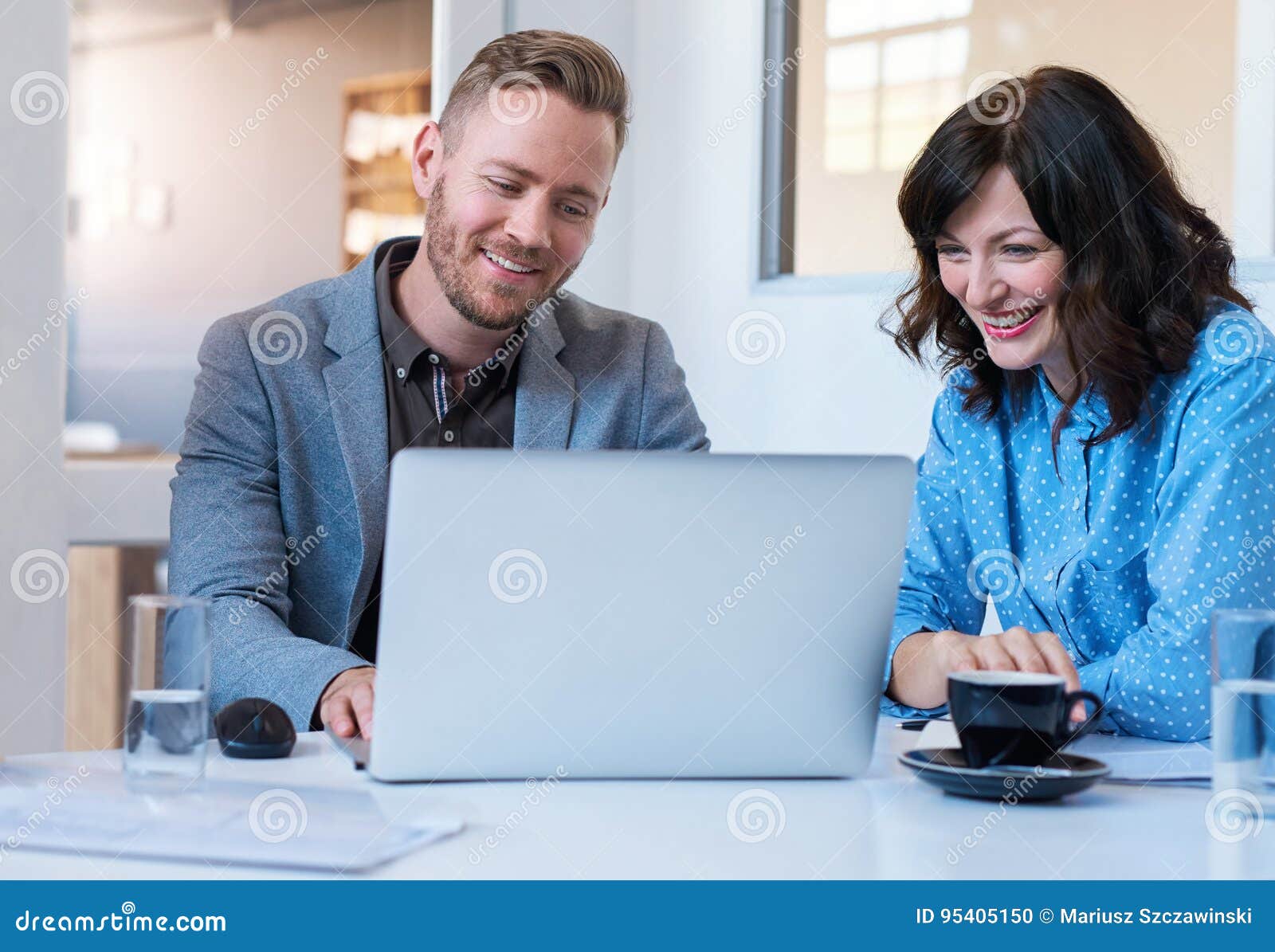 Two Smiling Young Coworkers Using a Laptop in an Office Stock Photo ...