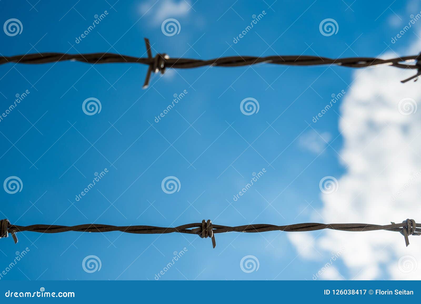 Two Strands of Barbed Wire with Blue Sky and Clouds in the Background ...