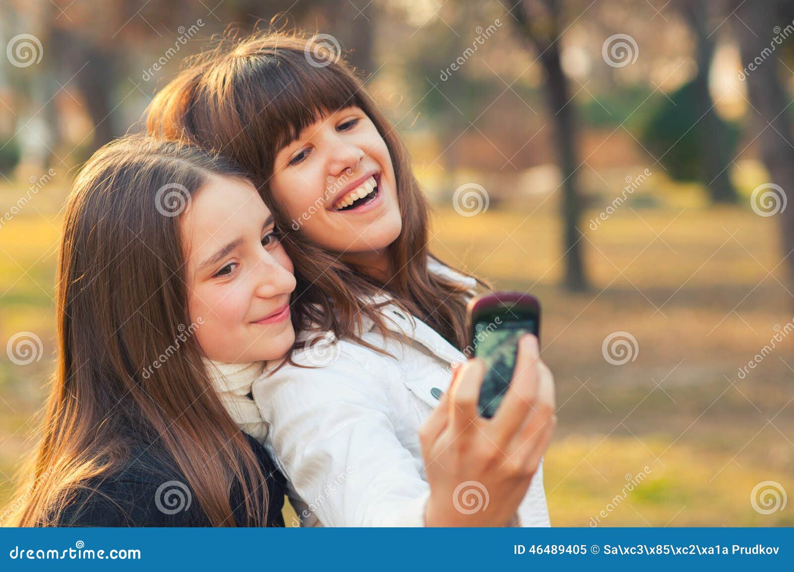 Two Teenage Girls Taking Selfies In The Park On Sunny Autumn Day Stock
