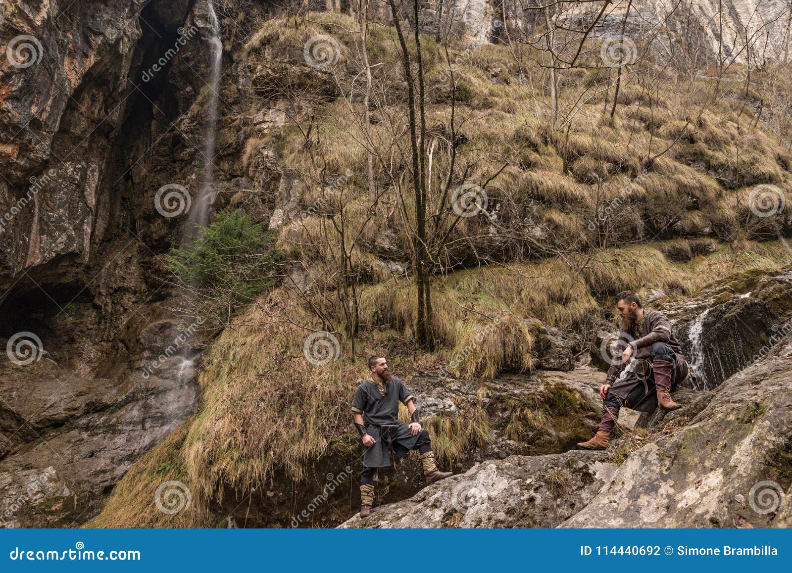 Two Viking Explorers Rest on the Rocks Next To a Waterfall in Th Stock ...
