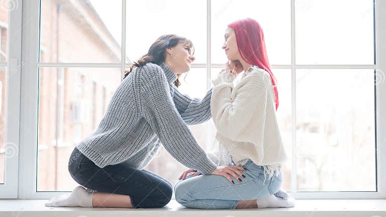 Two Women Dressed In Sweaters Sit By The Window And Gently Hug Lesbian
