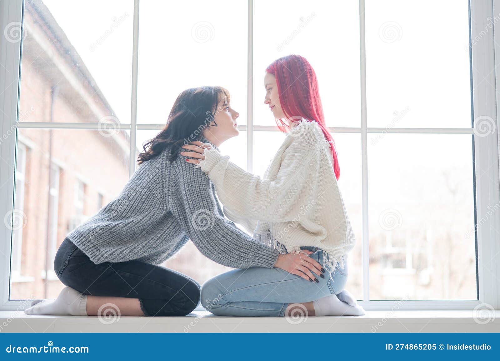 Two Women Dressed In Sweaters Sit By The Window And Gently Hug Lesbian