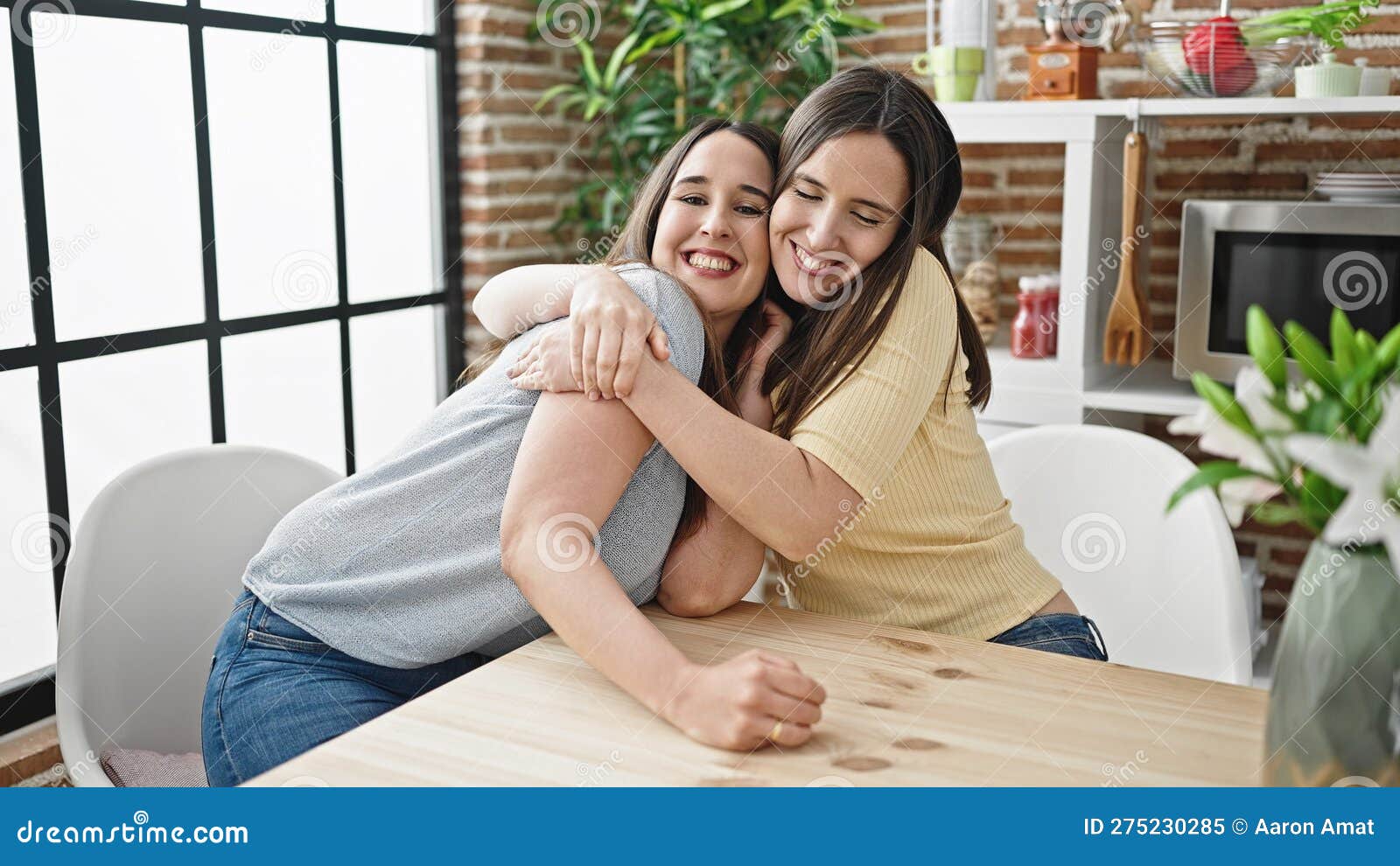 Two Women Hugging Each Other Sitting on Table at Dinning Room Stock ...
