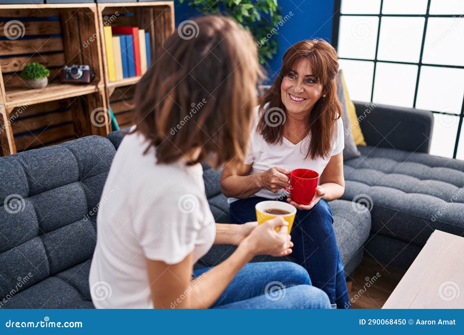 Two Women Mother And Daughter Drinking Coffee Sitting On Sofa At Home
