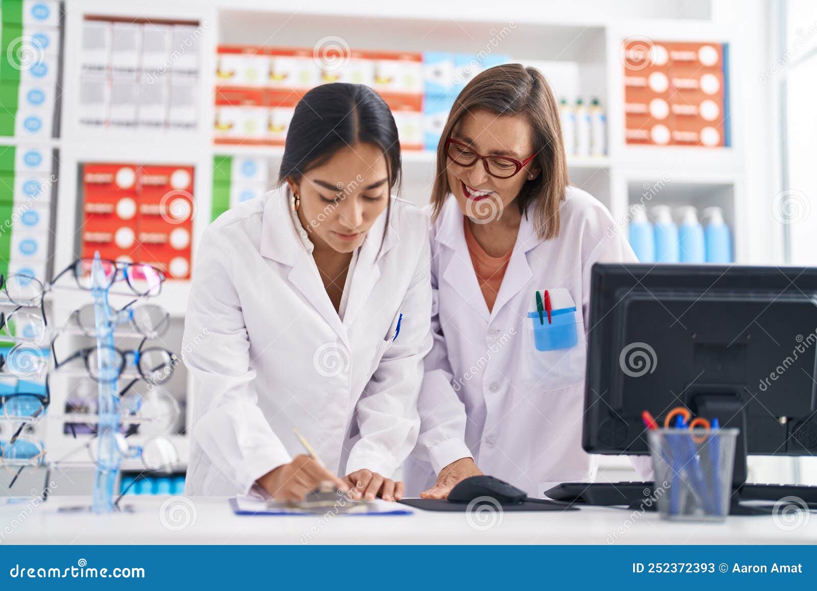 Two Women Pharmacist Smiling Confident Writing on Document at Pharmacy ...