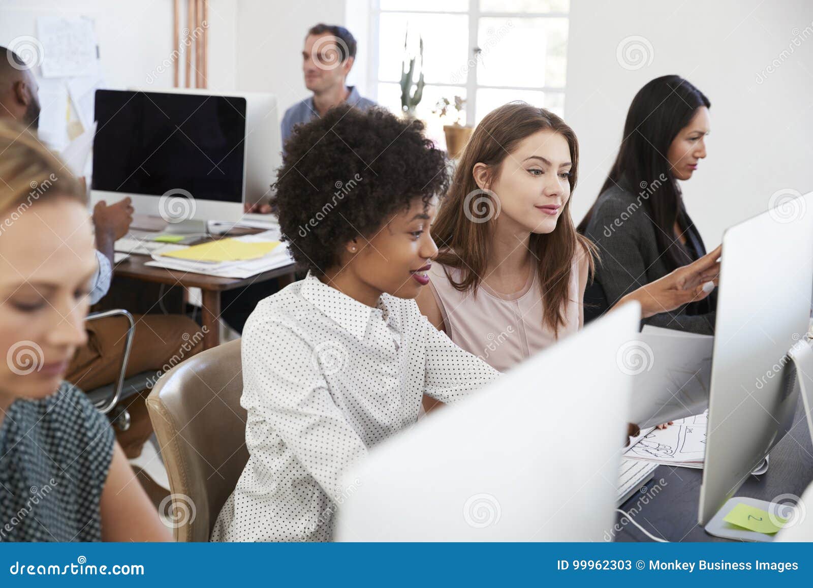 Two Women Sat at a Computer Discuss Work in Open Plan Office Stock ...