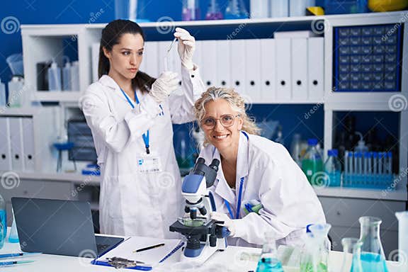 Two Women Scientists Using Microscope Measuring Liquid at Laboratory ...