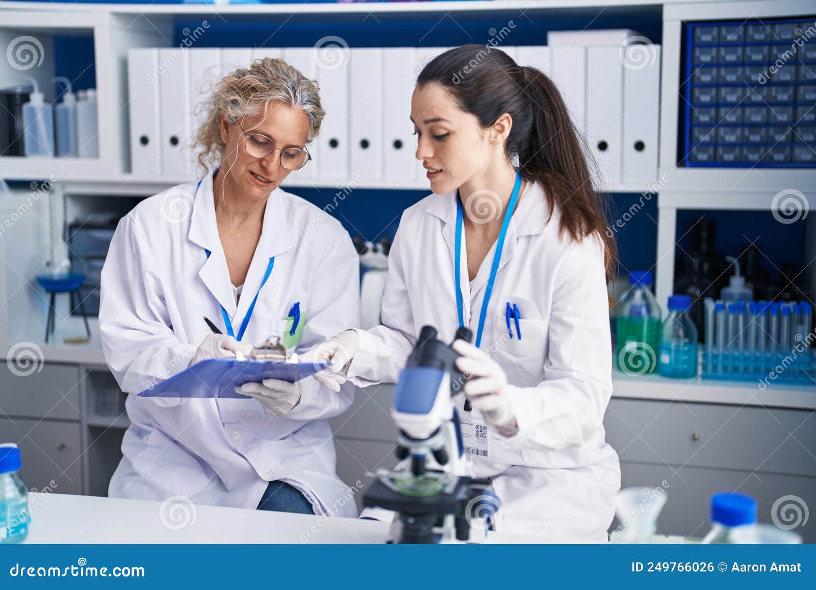 Two Women Scientists Using Microscope Write on Document at Laboratory ...