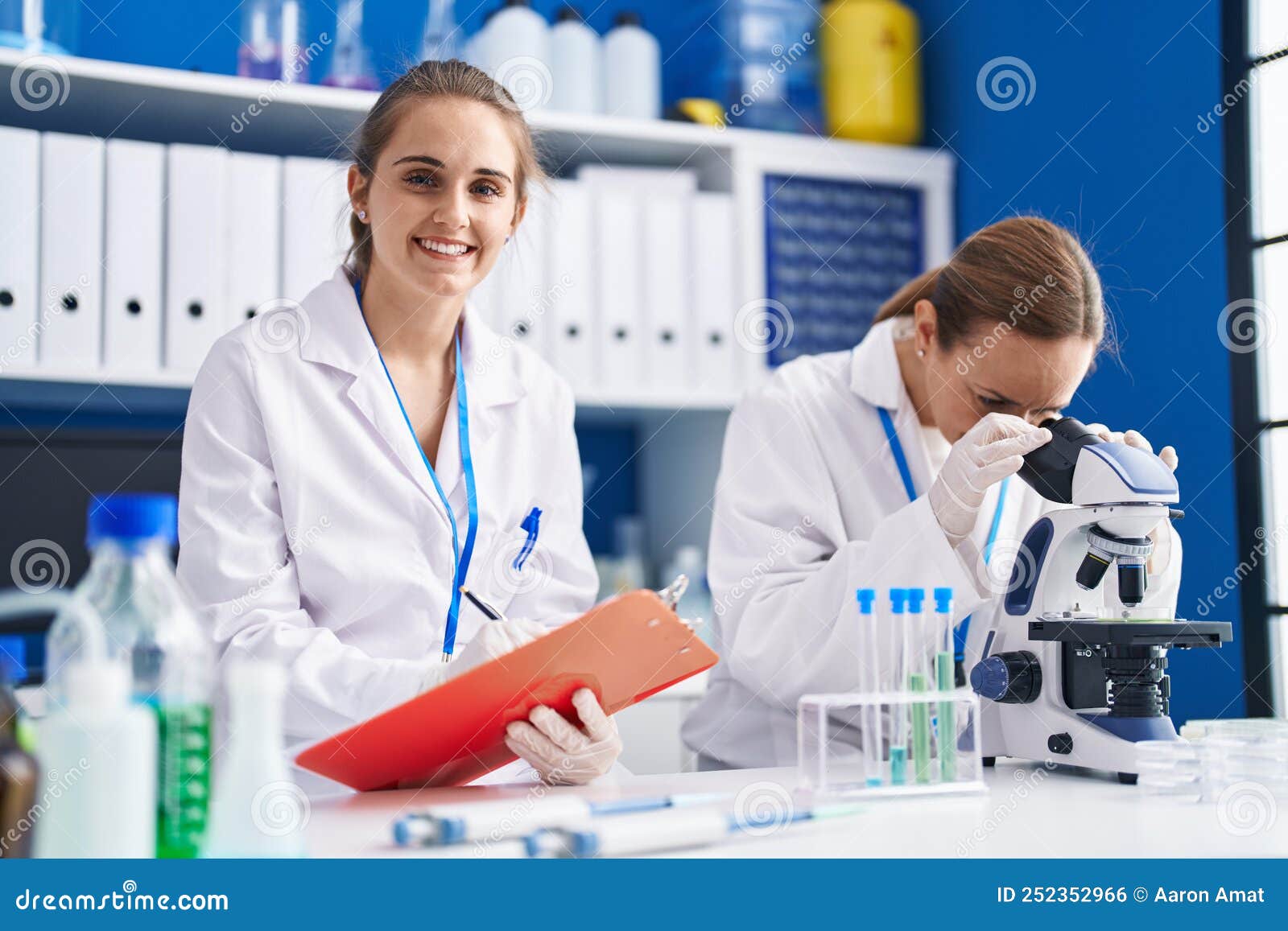 Two Women Scientists Using Microscope and Write on Document at ...
