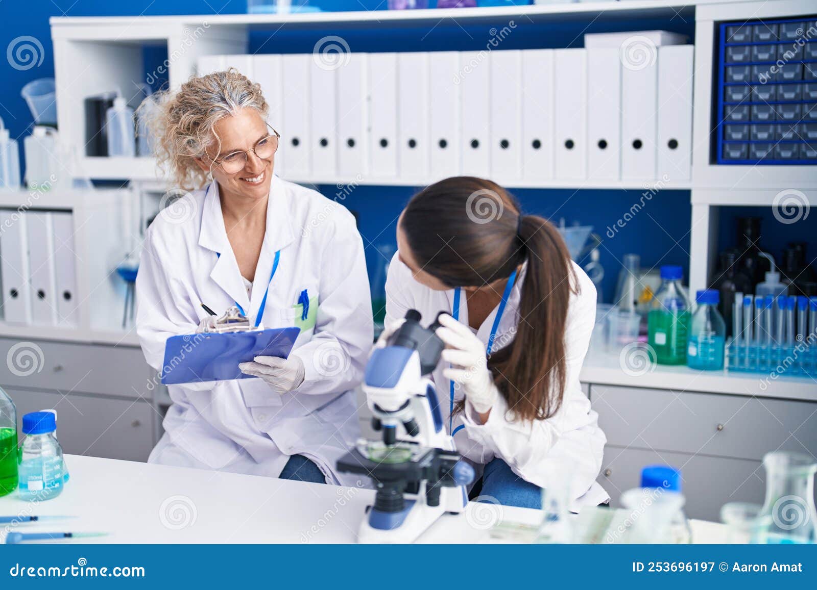 Two Women Scientists Using Microscope Write on Document at Laboratory ...