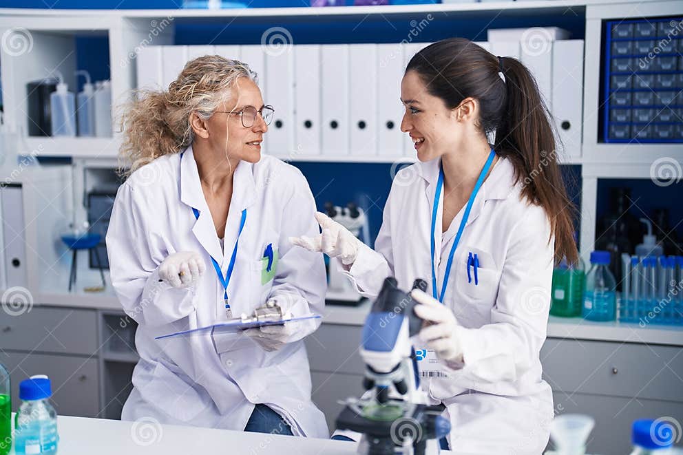 Two Women Scientists Using Microscope Write on Document at Laboratory ...