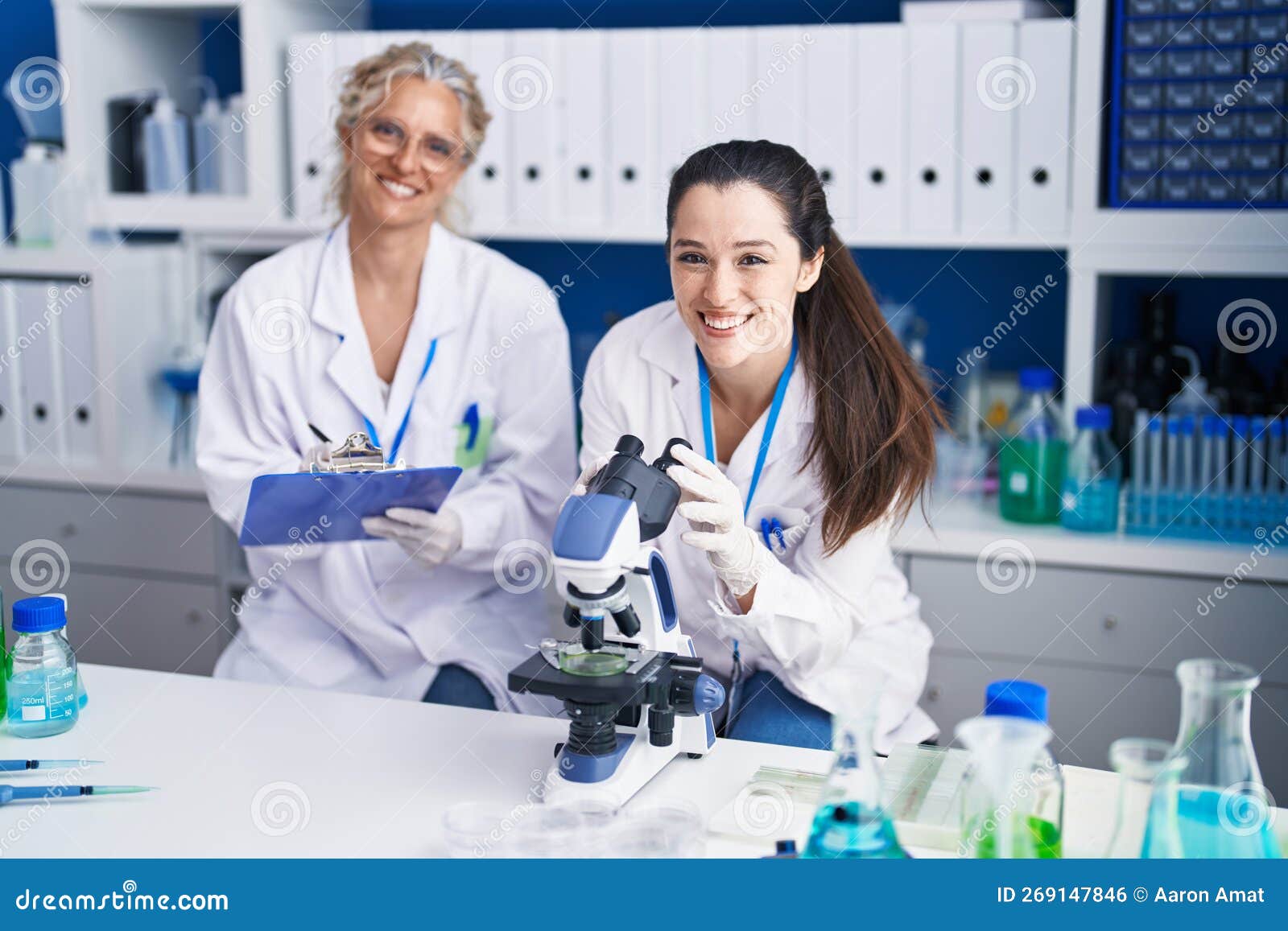 Two Women Scientists Using Microscope Write on Document at Laboratory ...