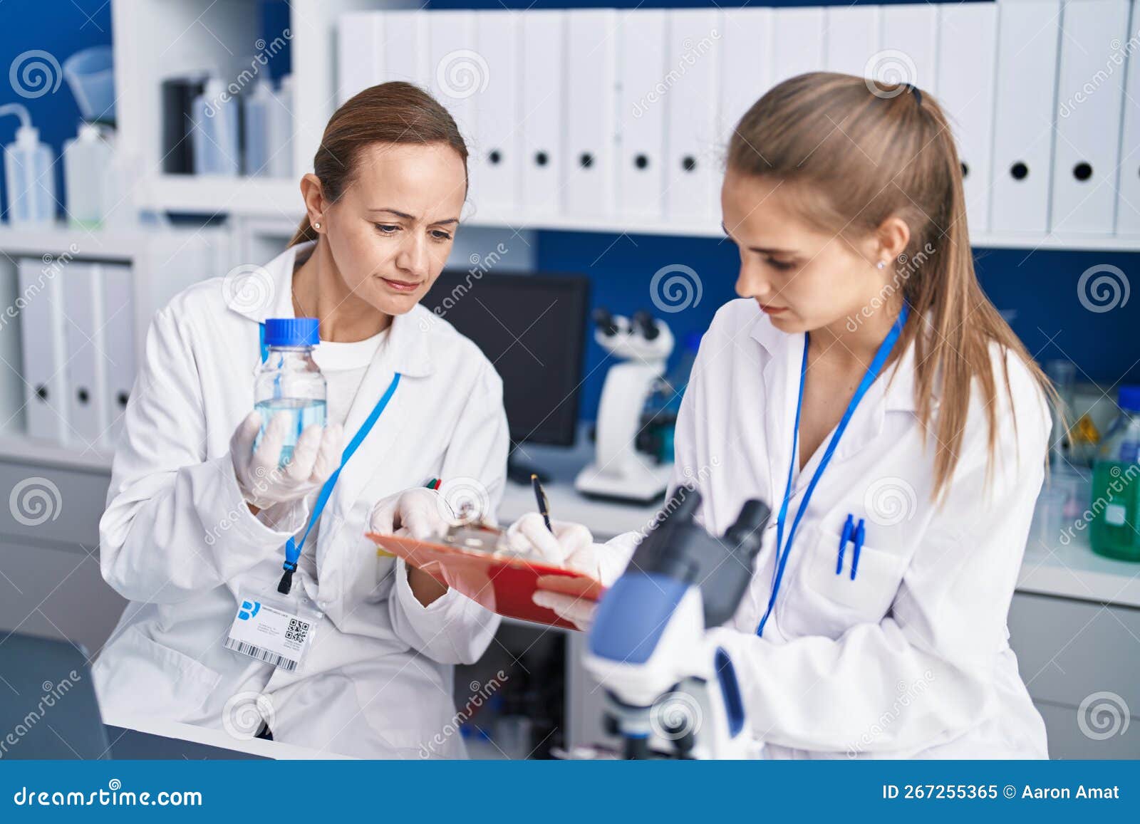 Two Women Scientists Write on Document Measuring Liquid at Laboratory ...