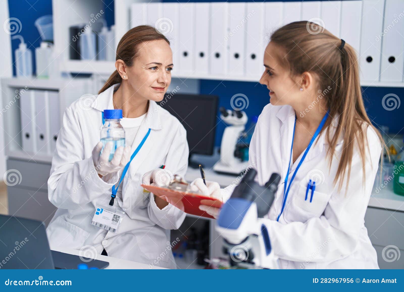 Two Women Scientists Write on Document Measuring Liquid at Laboratory ...