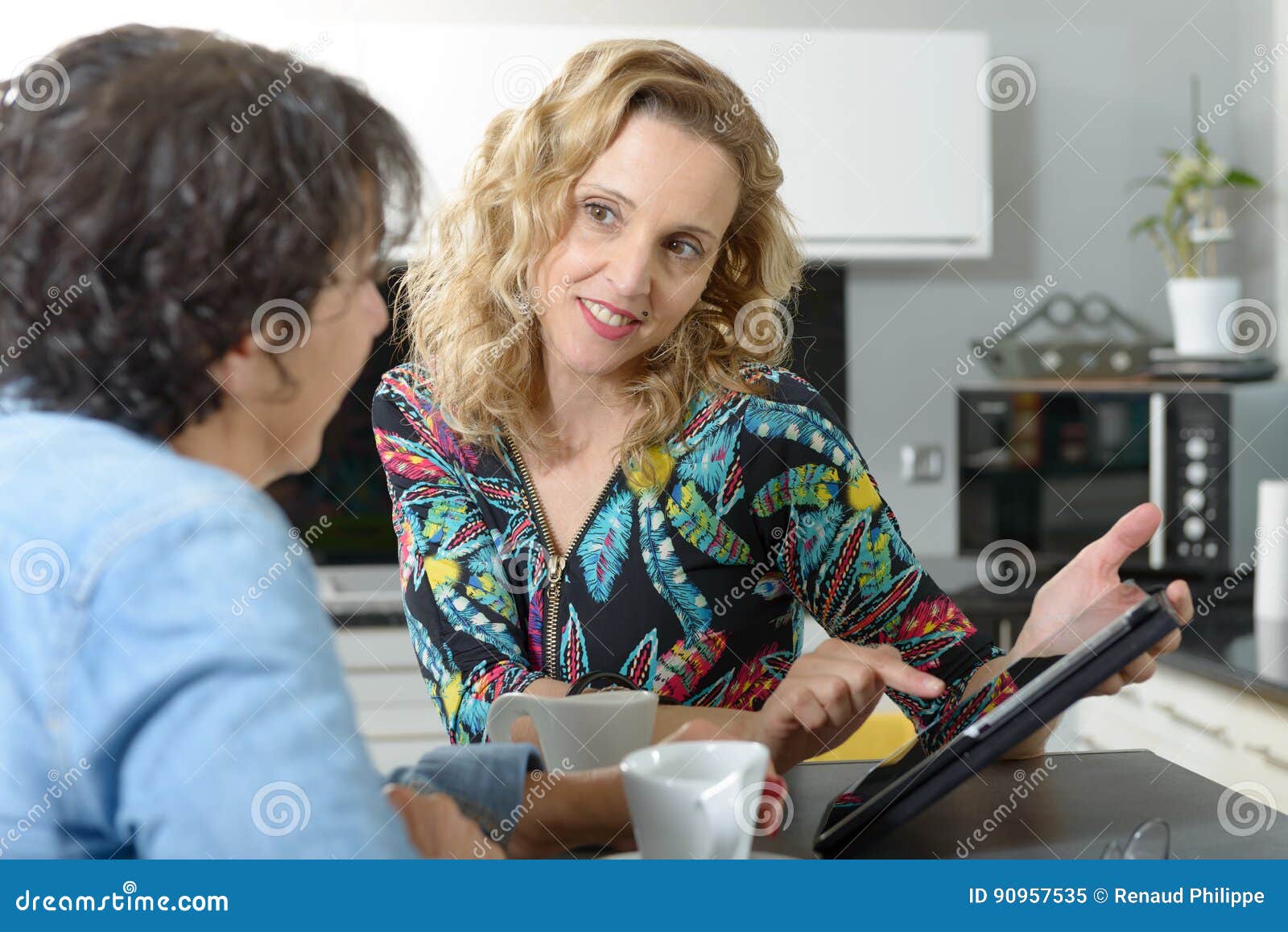 Two Women Sitting at Table in Kitchen and Using Tablet Stock Image ...