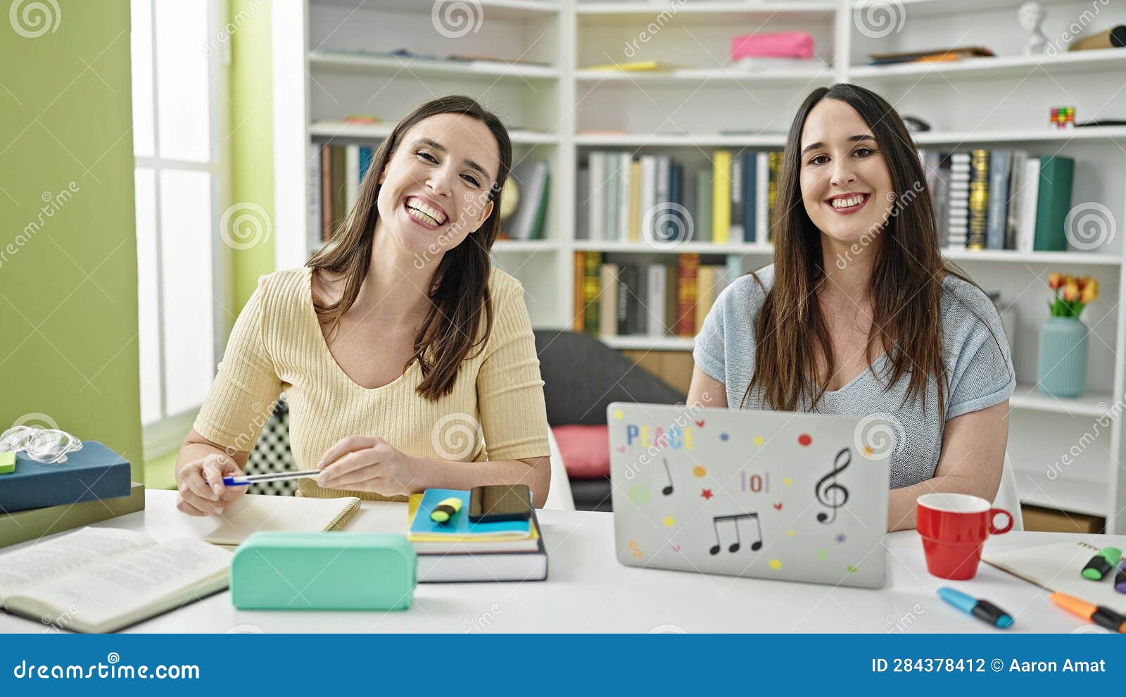 Two Women Sitting on Table Studying Using Laptop Writing Notes at ...