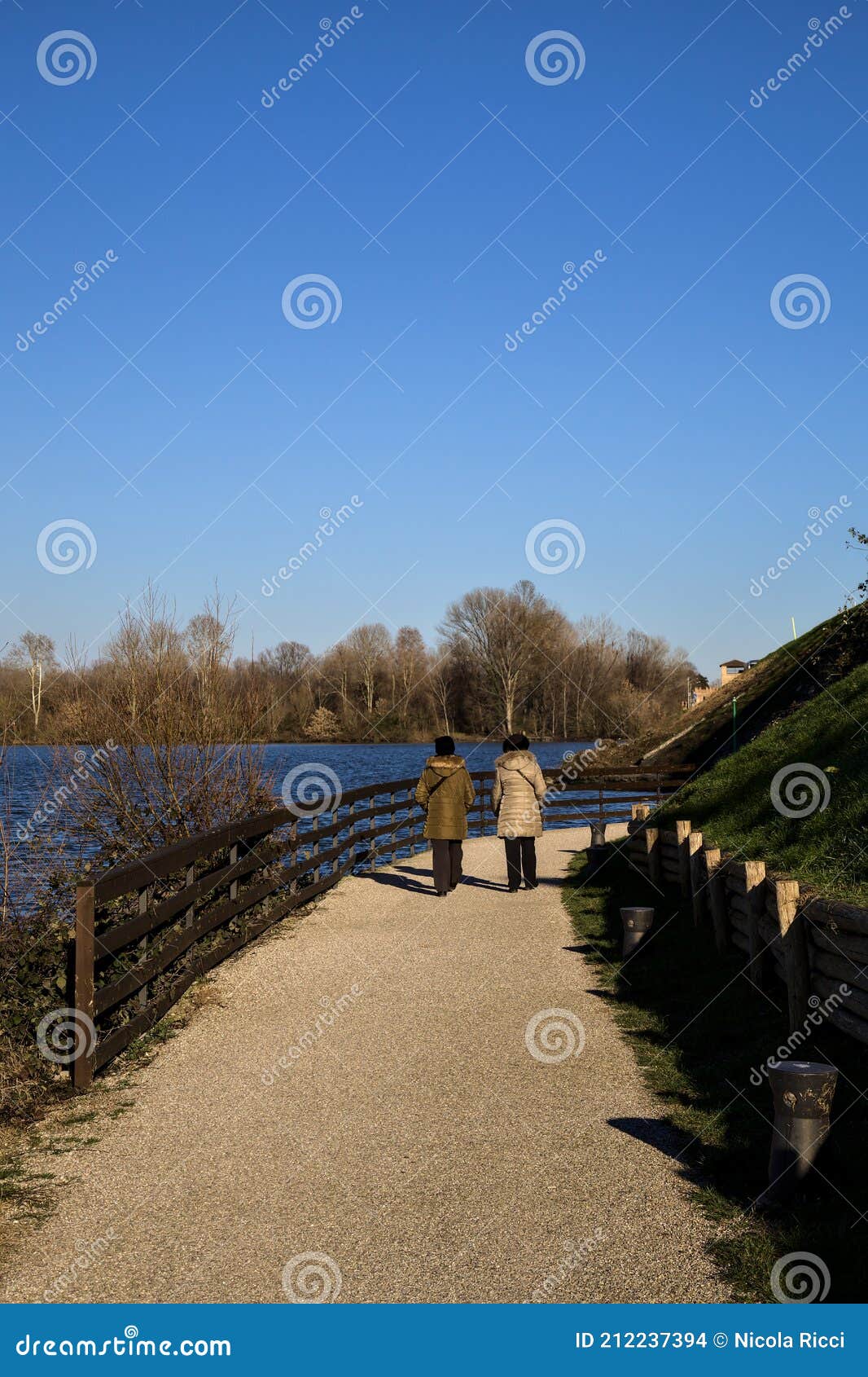 Two Women Walking on a Path by the Shore of a Lake at Sunset in Winter ...