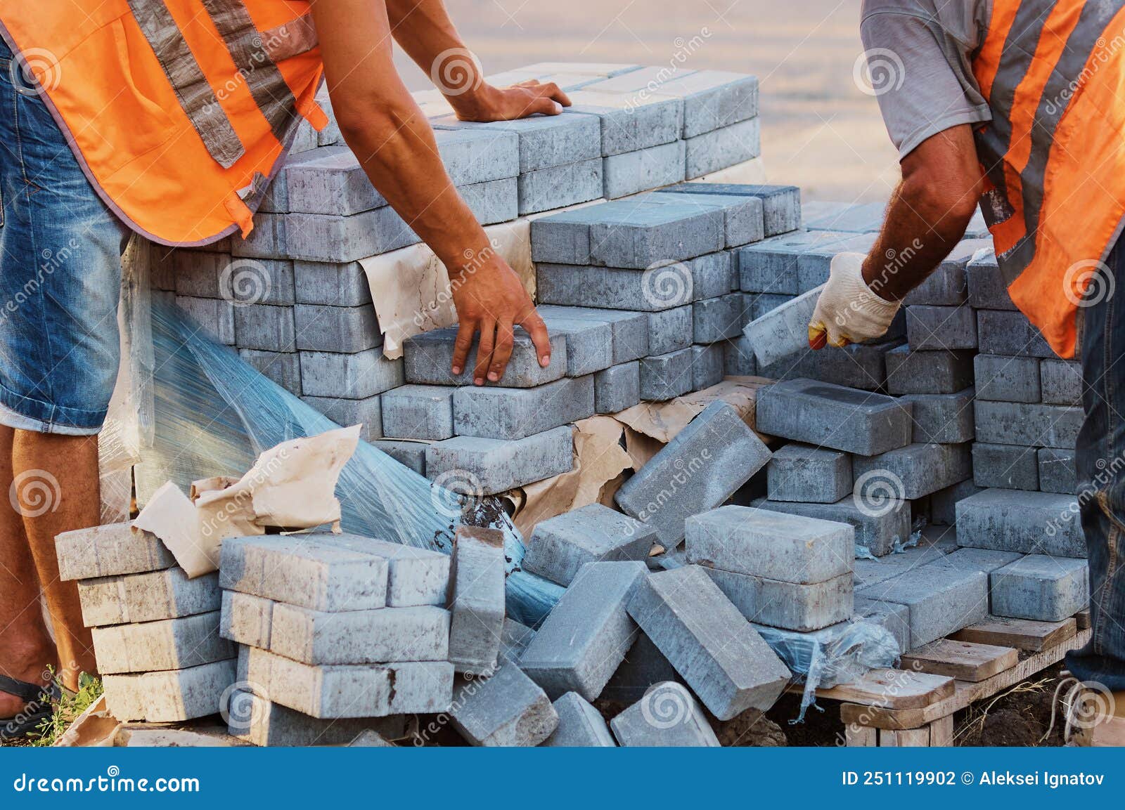 Two Workers in Orange Vests Stack Paving Slabs in a Compact Pile. Close ...