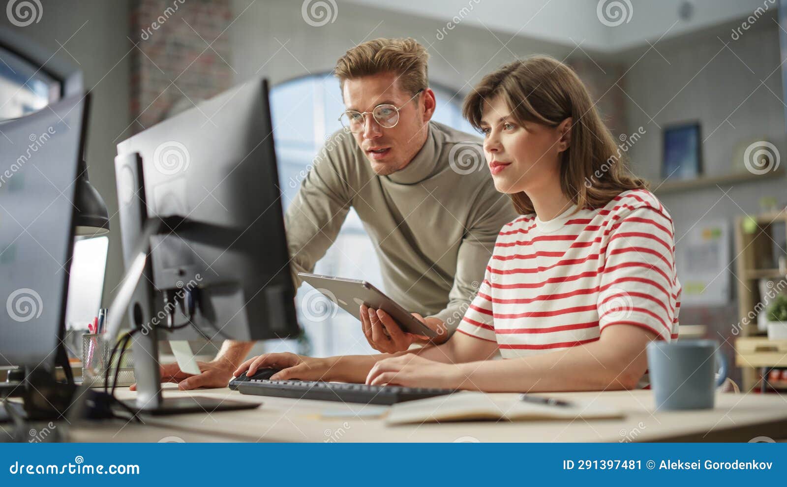 Two Young Creative Colleagues Discussing Work Project and Pointing at ...