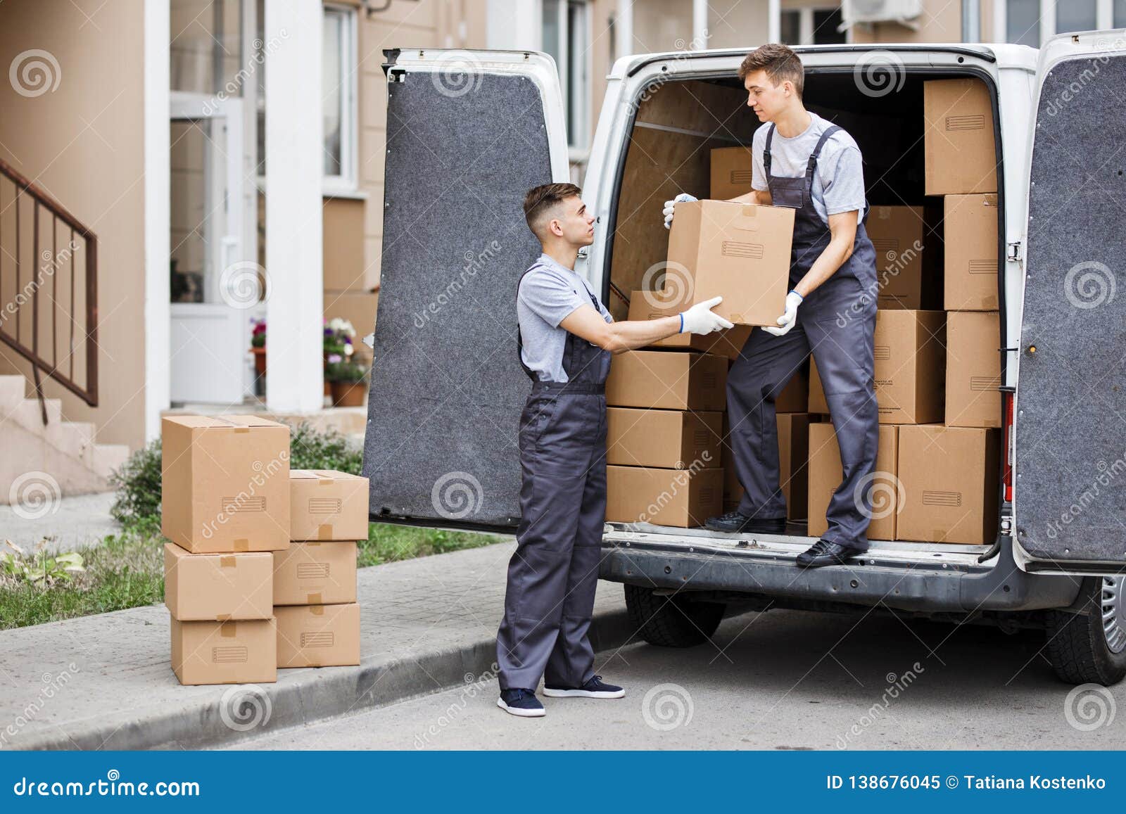Two Young Handsome Movers Wearing Uniforms are Unloading the Van Full ...