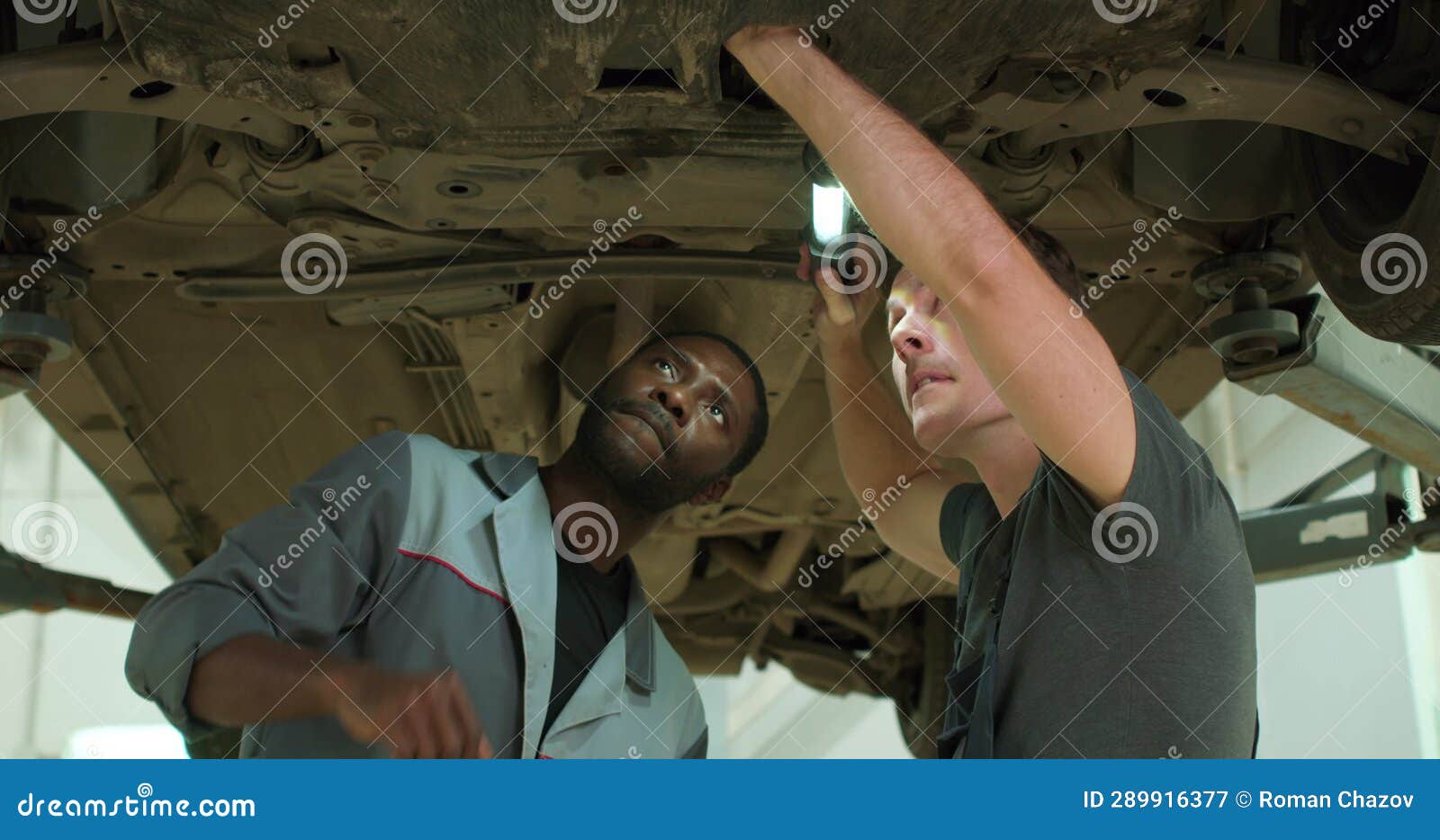 Two Young Hardworking Auto Mechanics Working on Undercarriage of Car ...