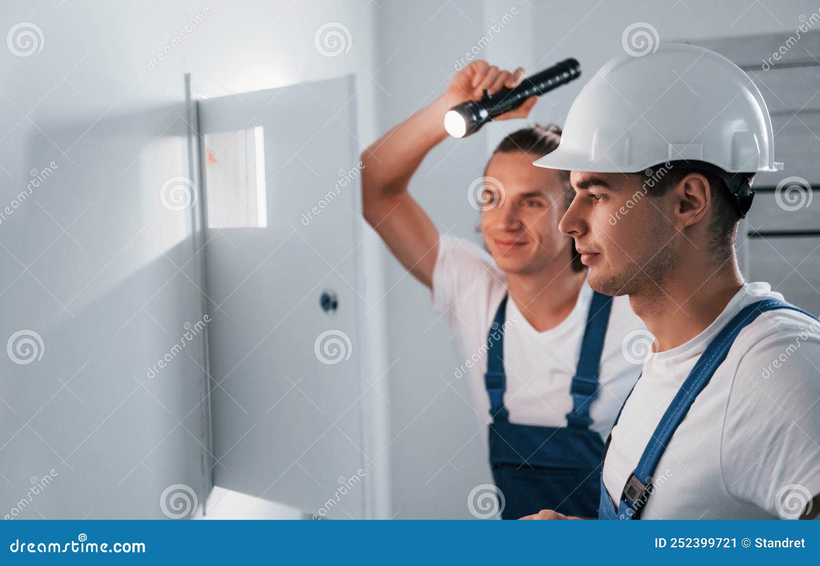 Two Young Male Electricians Works Indoors Together. Using Flashlight ...