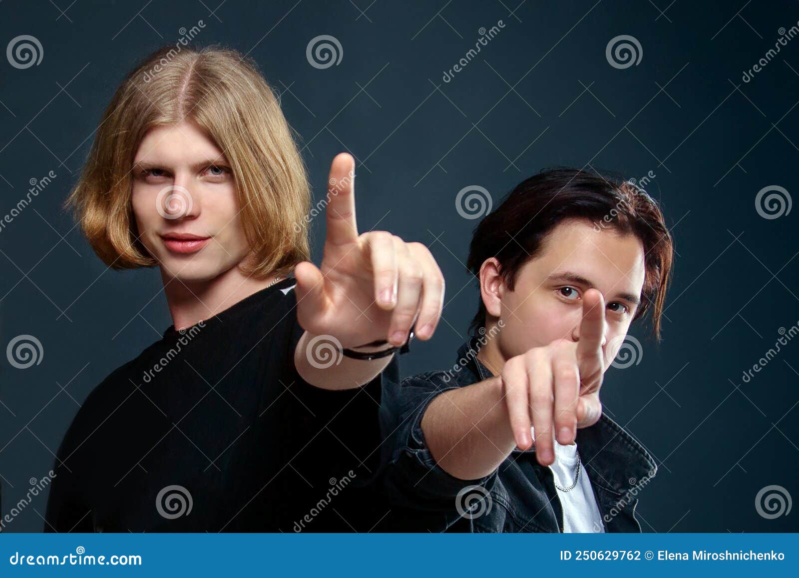 Two Young Men Standing Close To Each Other And Pointing Out Ahead With Fingers Smiling Stock