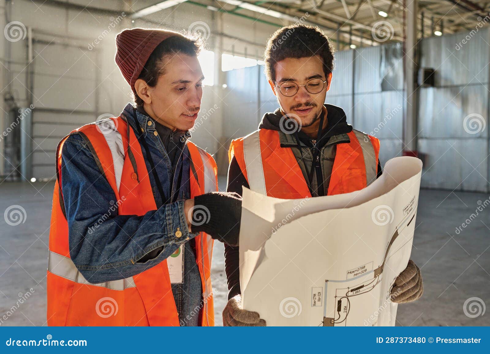 Two Young Multiethnic Engineers Looking at Building Plan on Blueprint ...