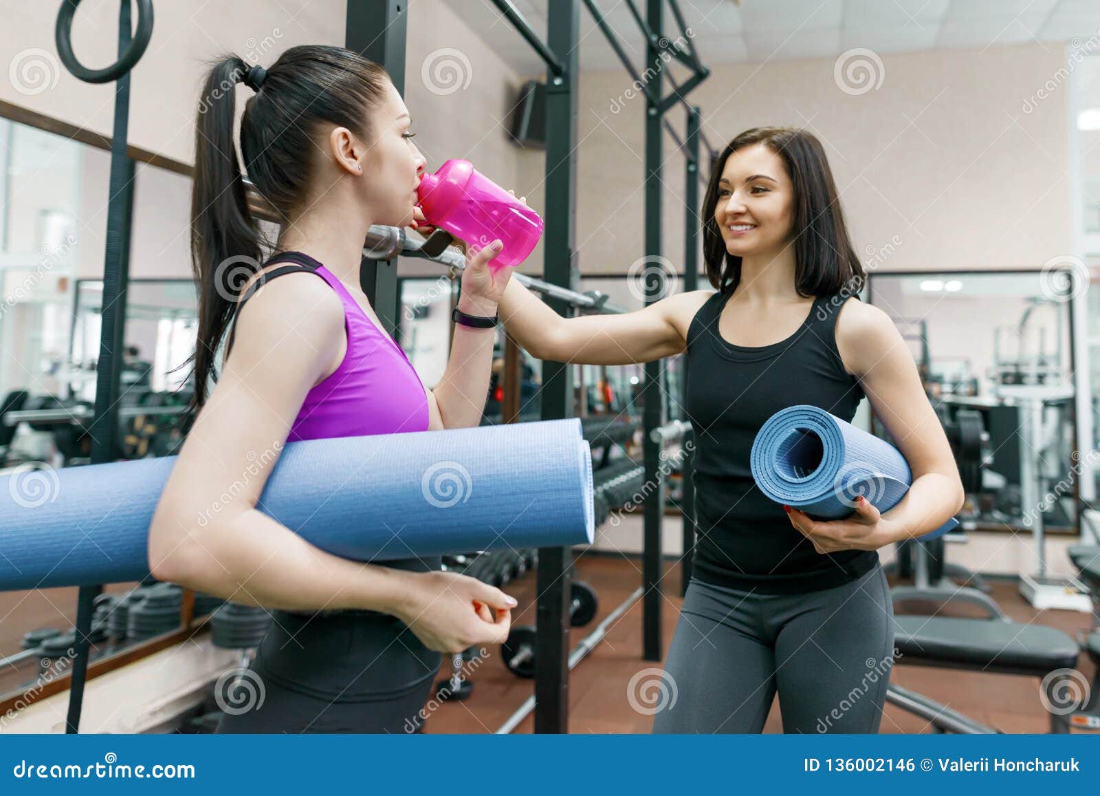 Two Young Smiling Fitness Women Talking With Sport Mats In The Gym