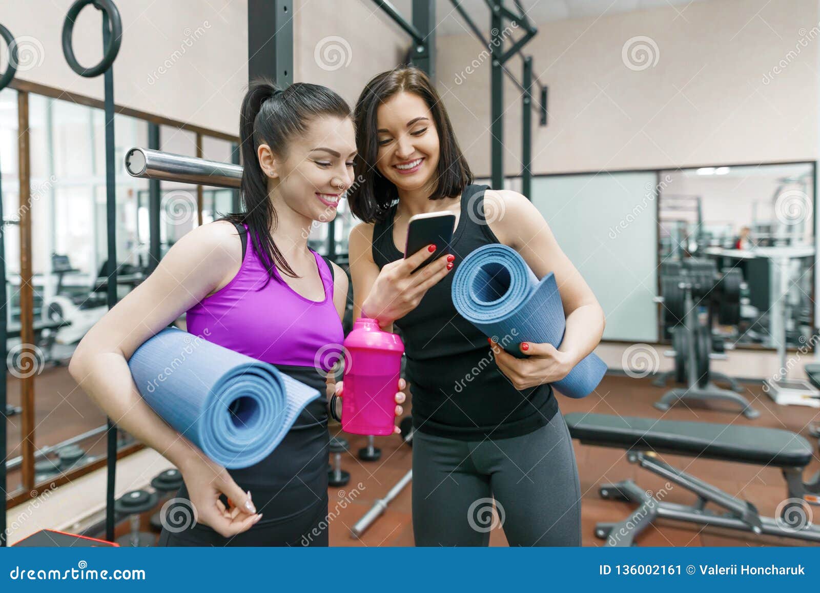 Two Young Smiling Fitness Women Talking With Sport Mats In The Gym