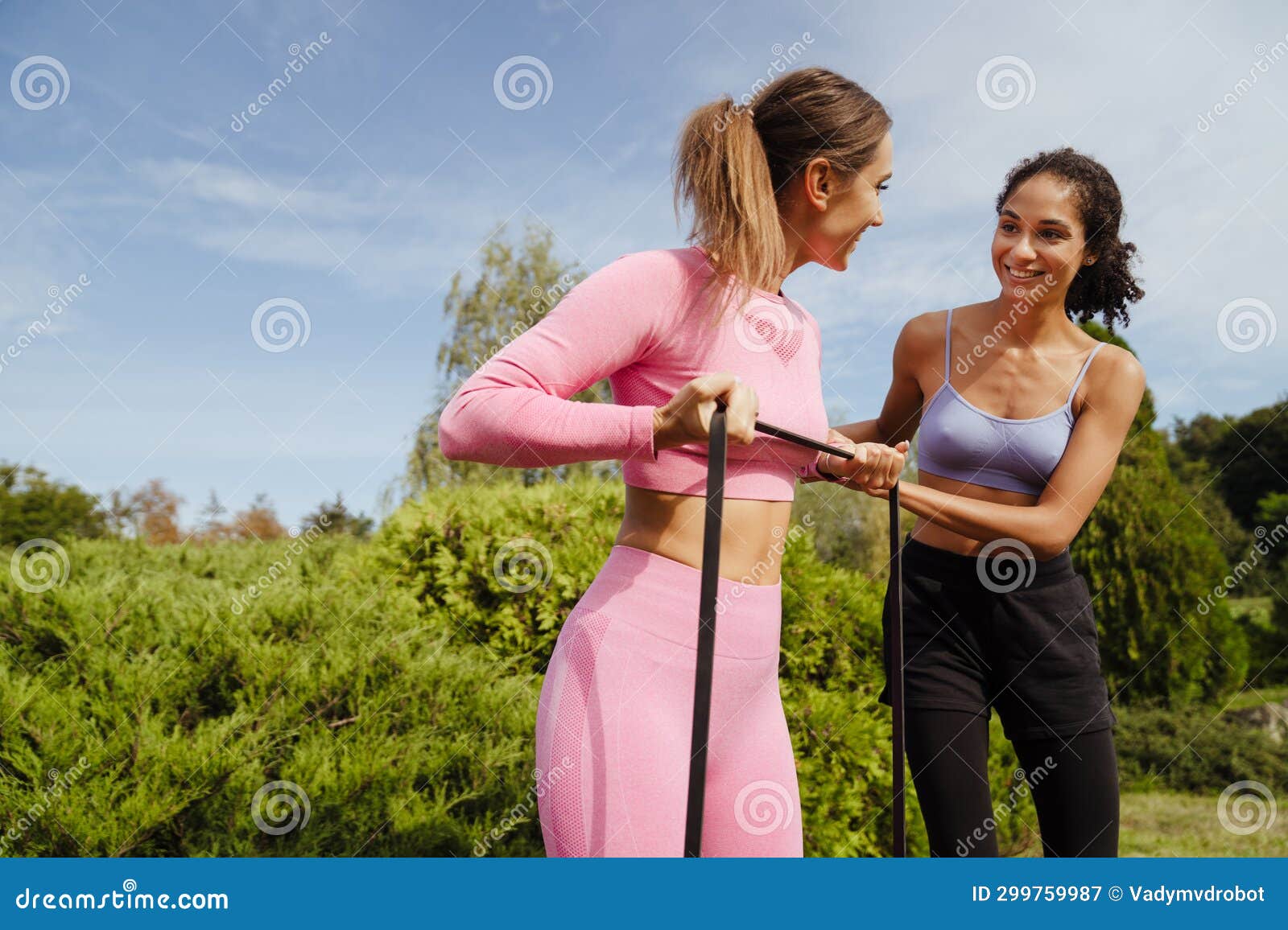 Two Smiling Women Doing Exercises With Resistance Band In Park Stock