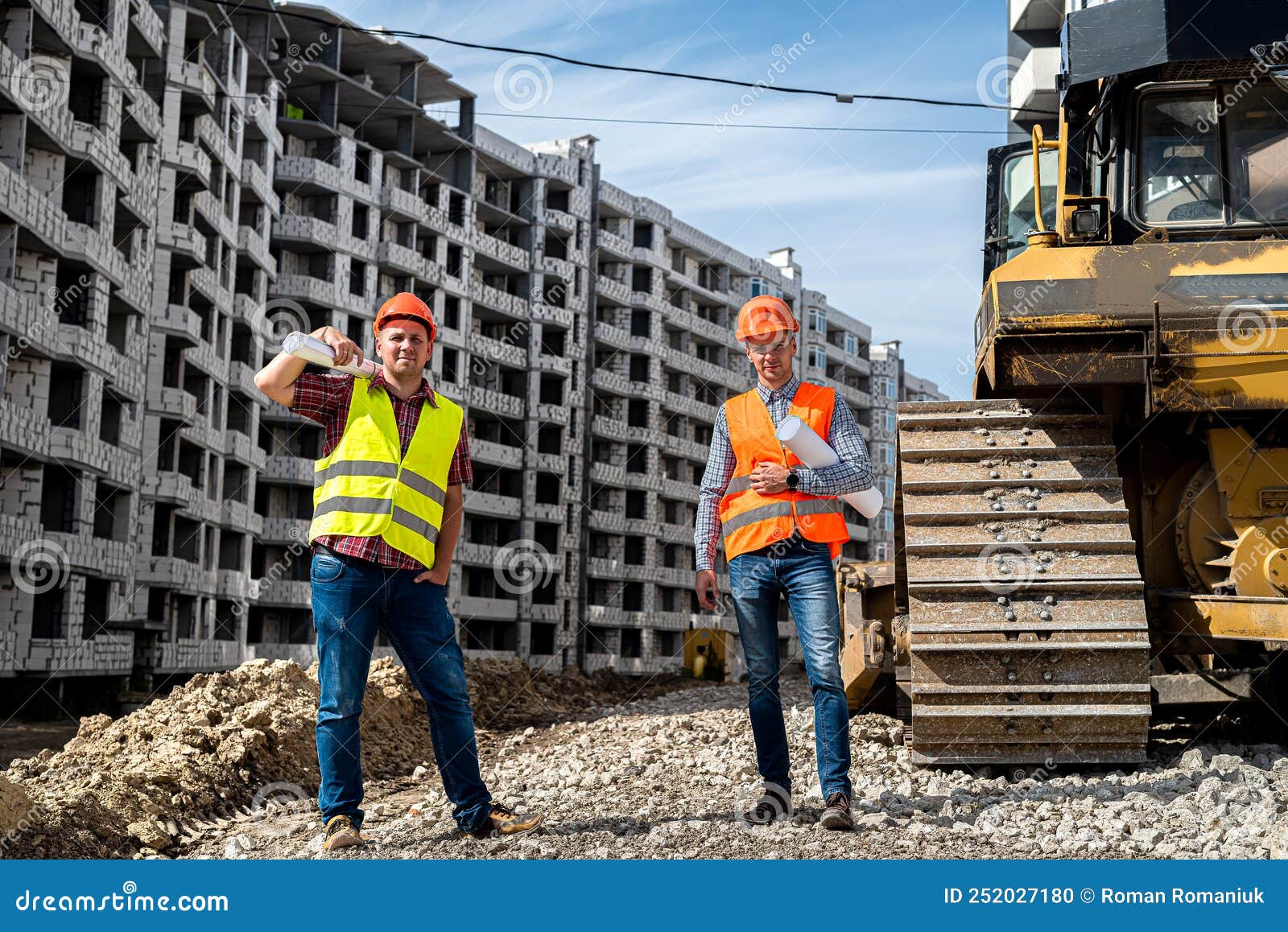 Two Young Strong Workers in Uniform and Helmets Stand Near a Grader on ...
