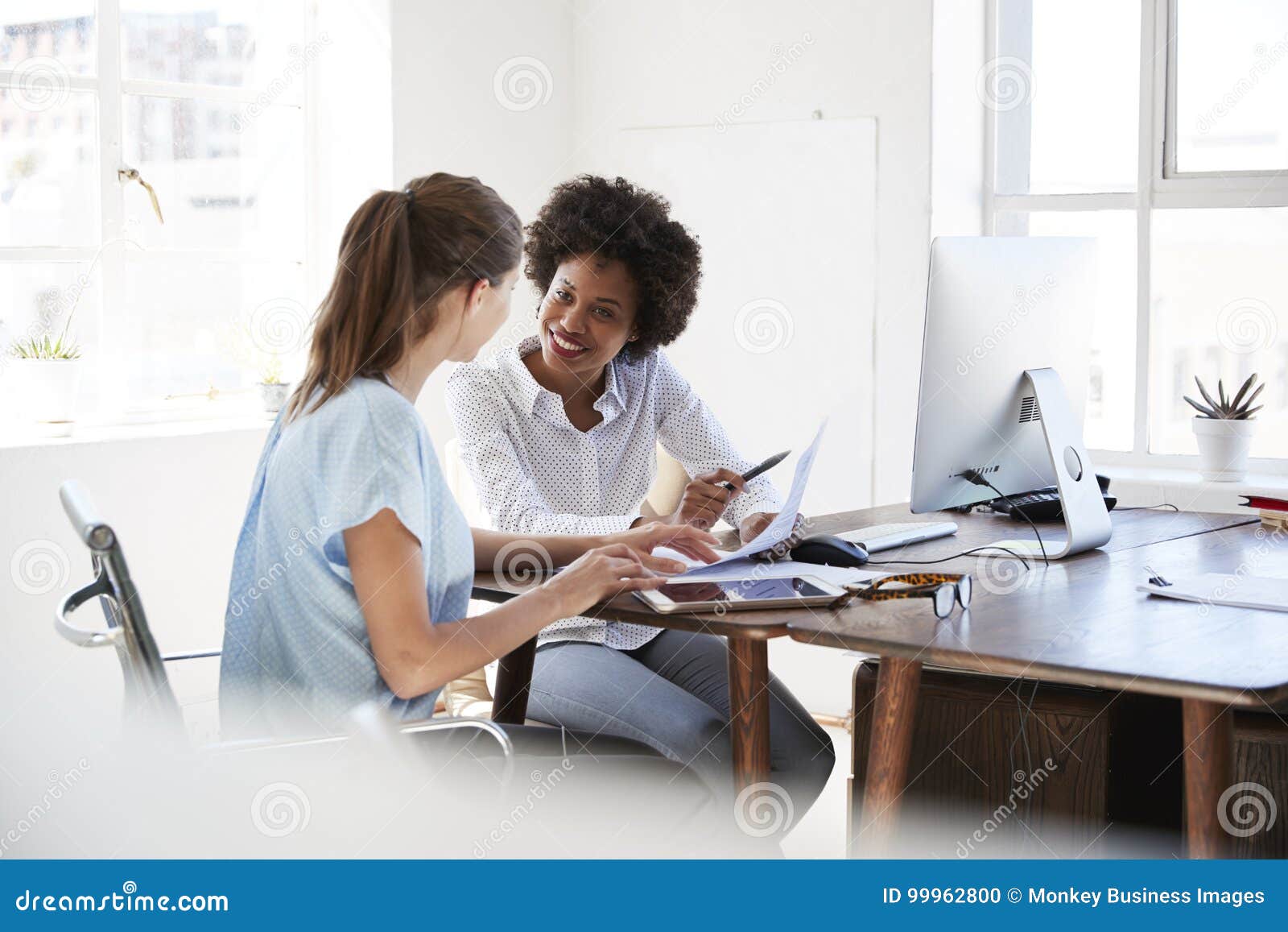 Two Young Women Discussing Documents at a Desk in an Office Stock Photo ...