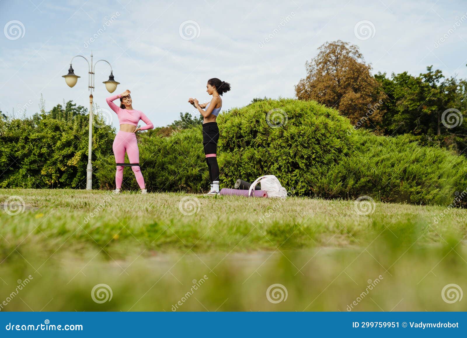 Two Young Women Doing Exercises With Resistance Bands In Park Stock