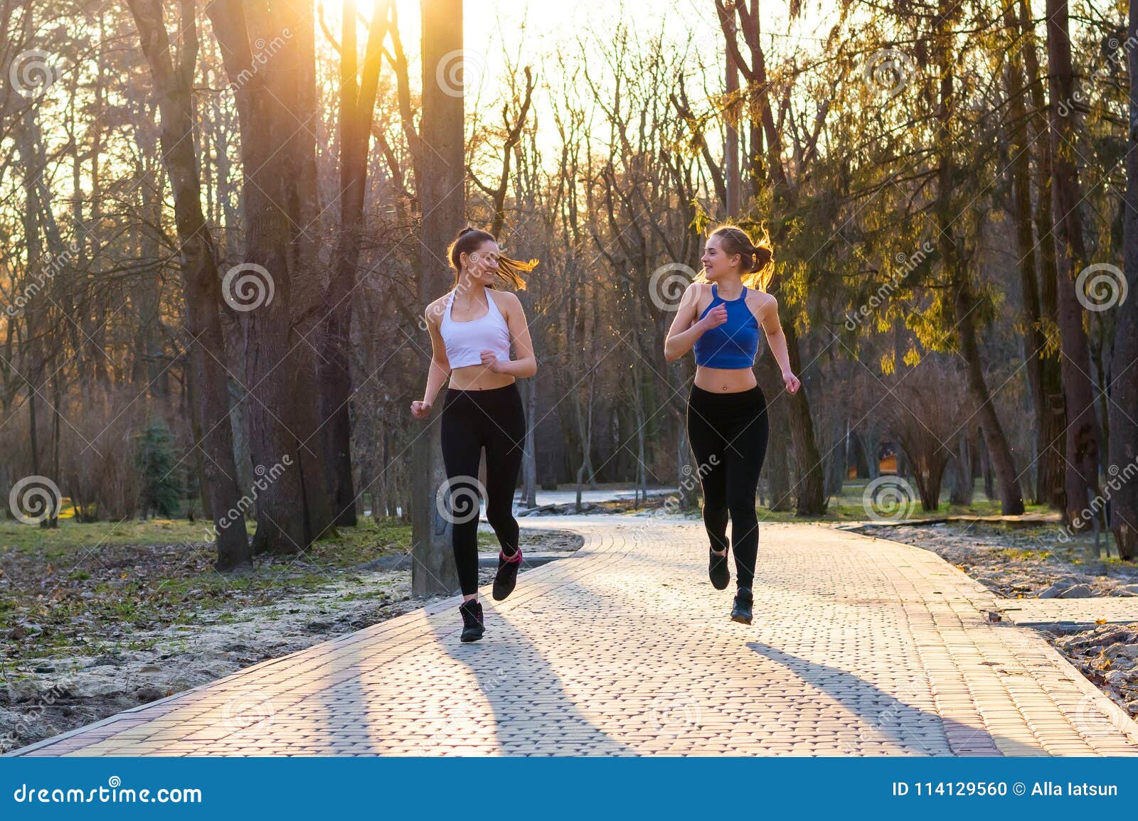 Two Young Women Run Along the Path in the Park at Sunset Stock Photo ...