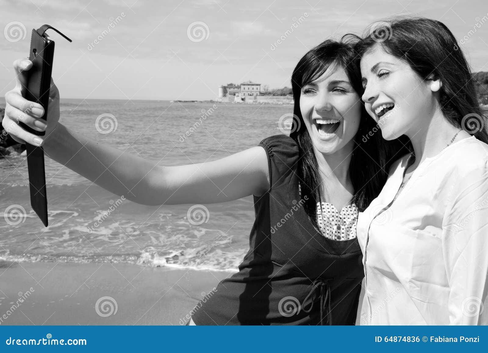 Two Young Women Taking Selfie In Front Of Beach Making Funny Faces