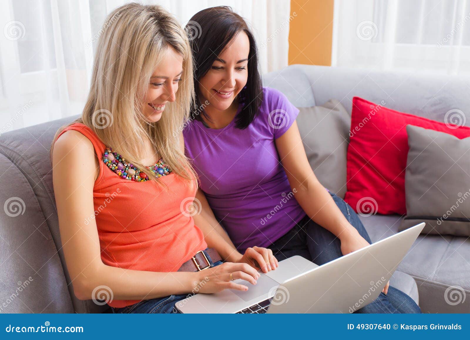 Two Young Women Using Computer while Sitting on Couch in Living Room ...