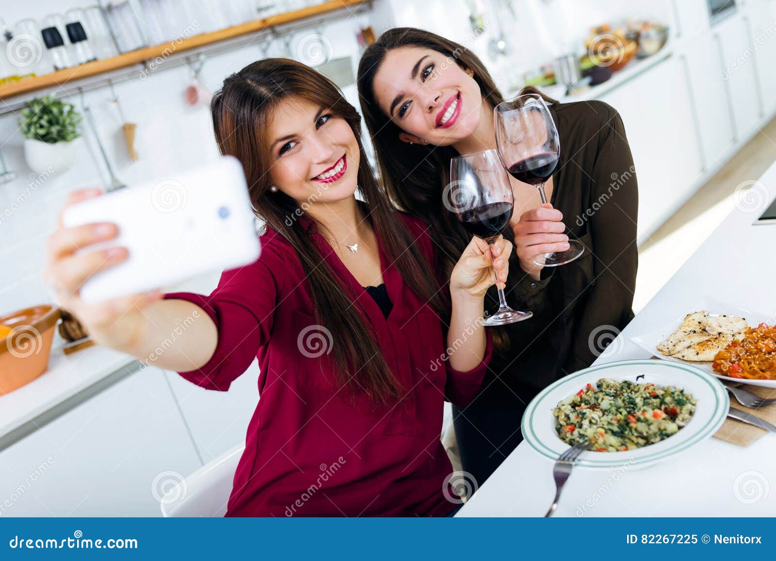 Two Young Women Using Mobile Phone while Eating in the Kitchen. Stock ...