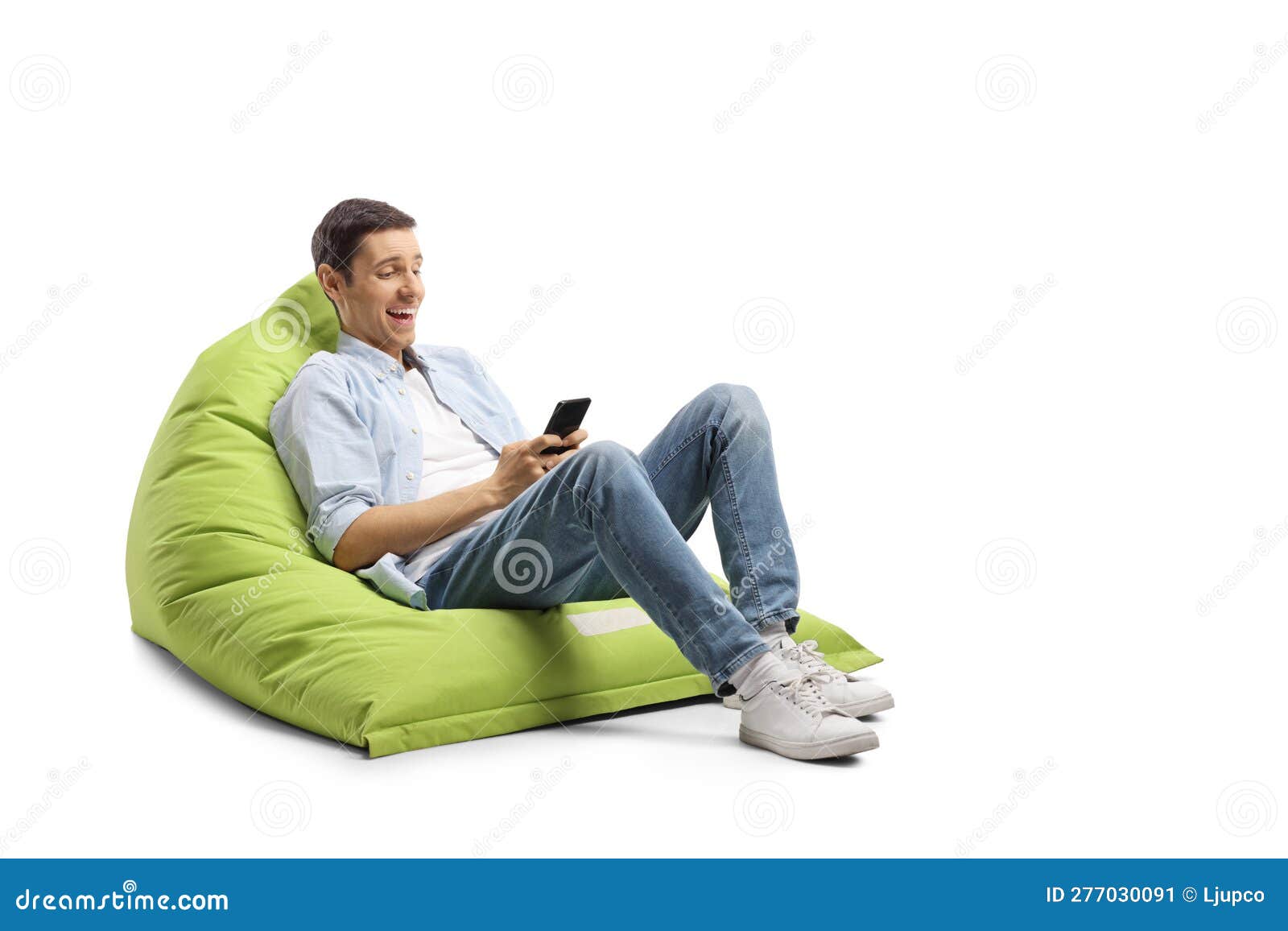 Un Joven Sentado En Una Bolsa De Frijol Riendo Y Mirando Un Smartphone ... Un Joven Sentado En Una Bolsa De Frijol Riendo Y Mirando Un Smartphone ...